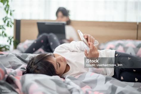 침대에서 혼자 웃는 얼굴로 스마트 폰에서 비디오를보고있는 귀여운 어린 아이 소녀 집에서 행복한 얼굴로 휴대 전화를 사용하는