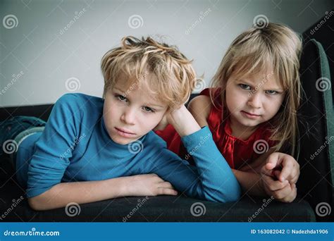 Bored Brother And Sister Sitting On Sofa And Holding Remote Control