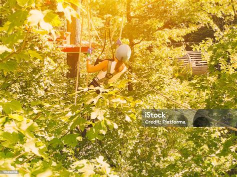 십대 소녀는 안전 장비와 헬멧을 착용 한 놀이 공원의 나무 사이의 로프 다리를 따라 걷습니다 나무 숲에있는 로프 공원 안전 스트랩과 보호 헬멧이 장착 된 모험 트랙에서