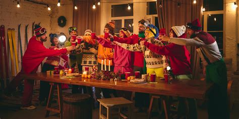 형형색색의 스키 장비와 축제 스웨터를 입은 쾌활한 친구들이 촛불이 켜진 장식된 나무 테이블 주변에서 음료를 마시며 실내에서 휴가 정신을 즐기고 있습니다 18 19세에 대한