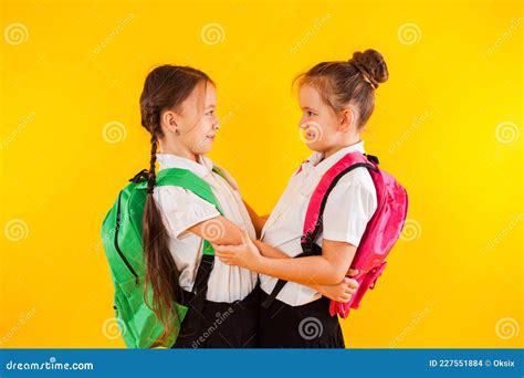 Two Smiling Schoolgirls In Uniform Are Hugging At The Yellow Stock