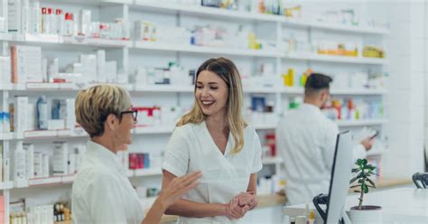 책상 근처에 서서 이야기하는 동안 선배 동료와 함께 일하는 행복한 젊은 여성 약사 사진 Unsplash의 약국 이미지