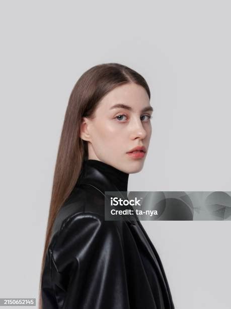 거대한 파란 눈과 예쁜 얼굴을 가진 아름 다운 젊은 여성이 세련된 검은 가죽 블레이저 재킷과 터틀넥을 입고 카메라를 보고 있습니다 긴 스트레이트 브라운 헤어 완벽한 내추럴