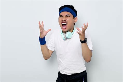 Molesto joven deportista asiático en diadema azul y camiseta blanca con