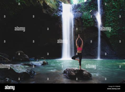 Young Women Meditate While Doing Yoga At The Waterfall In The Forest
