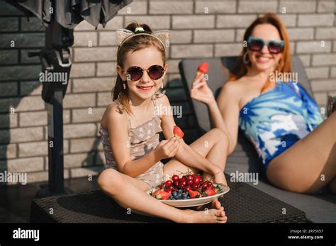 Mom And Daughter In Swimsuits Sunbathe In The Summer On Their Terrace