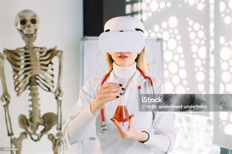 身著實驗室外衣的漂亮白種女性科學家的肖像在實驗室房間裡戴著vr眼鏡手裡拿著裝有紅色液體血液樣本或新物質的燒瓶背景上的人類骨架 照片檔及更多