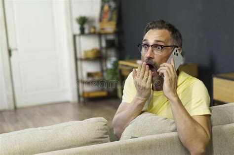 Handsome Man On Sofa Looks Shocked Talking Over Smart Phone Stock Image