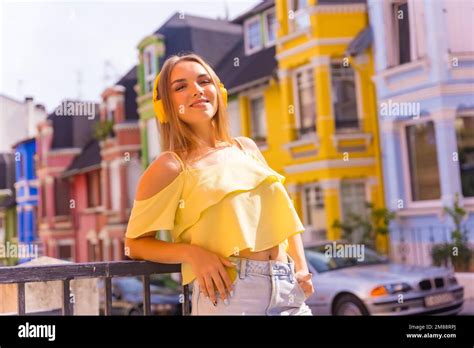 Young Blonde Woman In A Street With Houses With Colorful Facades Behind