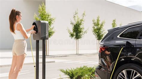 Girl Plugging Cable Charger Into Her Electric Car On Parking Stock