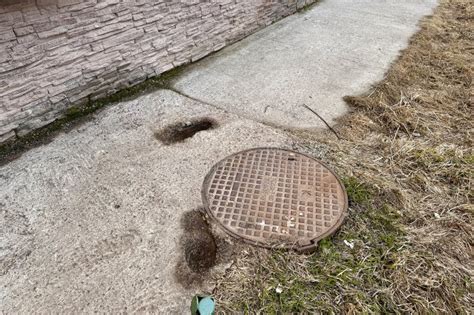 A Rusty Iron Hatch With A Pattern Is Mounted In The Asphalt Pavement Of