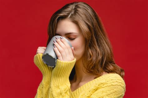 스튜디오에서 아름다운 여자는 잡고 머그잔에서 음료를 마시는 빨간 배경에 사람들과 개념 사람은 노란색 점퍼와 미소를 착용 컵에 커피 또는 차를 가진 소녀 18 19세에 대한