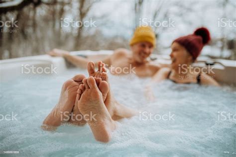 추운 겨울날 테라스에서 야외 욕조를 함께 즐기는 꼬인 모자를 쓴 시니어 커플 올라간 발에 대한 스톡 사진 및 기타 이미지
