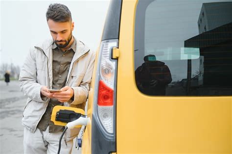 스마트폰으로 충전하고 시간을 조정하는 전기 자동차 근처에 서 있는 수염 난 백인 남자 남자에 대한 스톡 사진 및 기타 이미지 남자 전기 자동차 대체 연료 자동차 25