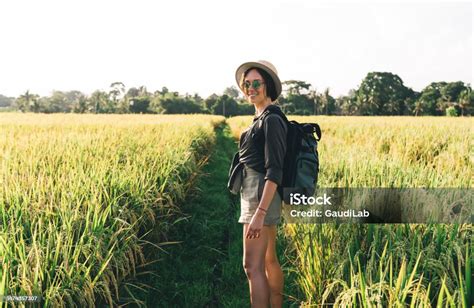 밀 수확과 함께 들판 근처에서 포즈를 취하는 여행 배낭을 멘 캐주얼 옷차림의 관광객의 절반 길이는 시골을 방문하기 위한 자유 시간을 즐기고 여름 햇살 동안 카메라를 향해