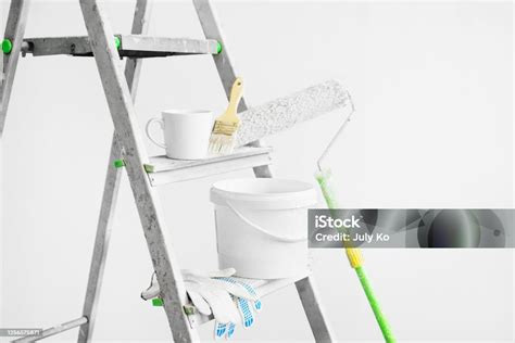 벽에 그림을 그리기 위한 도구 롤러 트레이 페인트 양동이 브러시 장갑 흰색 으로 칠해진 벽 근처의 사다리에 커피 한 잔 홈 리노베이션 기간 동안 커피 휴식 공간을 복사합니다
