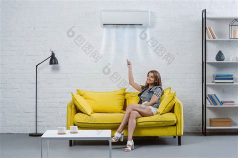 有吸引力的年轻妇女指向空调垂悬在墙壁与遥图片 包图网企业站