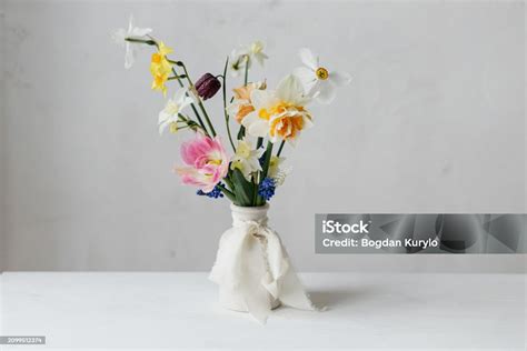 세련 된 봄 꽃 꽃병 와 리본 정물화 와 아름 다운 수선화와 튤립이 소박한 흰색 테이블에 부드러운 꽃다발 텍스트를 위한
