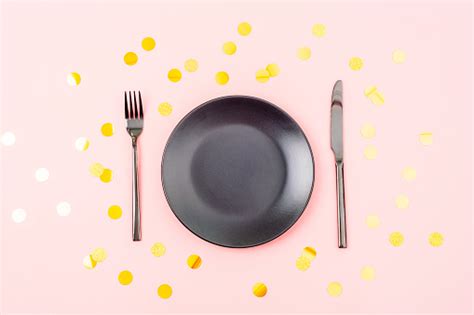 검은 접시가 있는 세련된 테이블 세팅 황금색 색종이 조각이 있는 분홍색 배경에 칼붙이 크리스마스 생일 휴일 개념 평면도 플랫