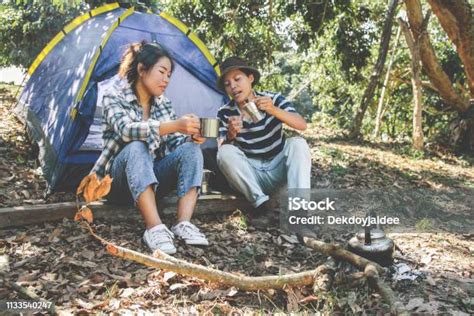 행복 한 미소 젊은 아시아 남자와 여자 타탄 셔츠에 앉아 친구의 이야기와 텐트 밖에 서 커피를 마시는 그룹 릴랙스 캠핑 인
