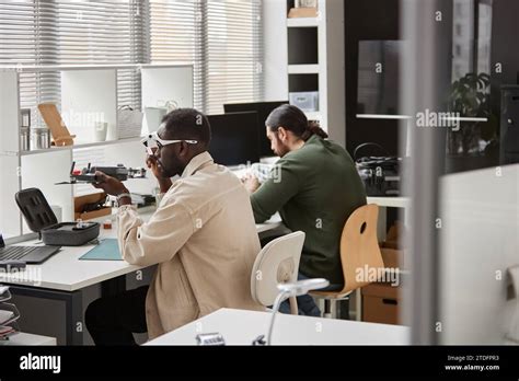 Back View At Two People Fixing Electronics Sitting At Workstation In