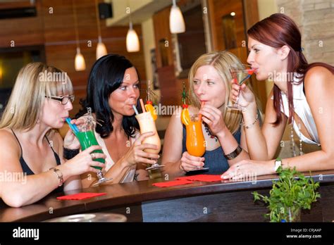 Four Young Women Sitting At The Bar Drinking Cocktails Together Stock