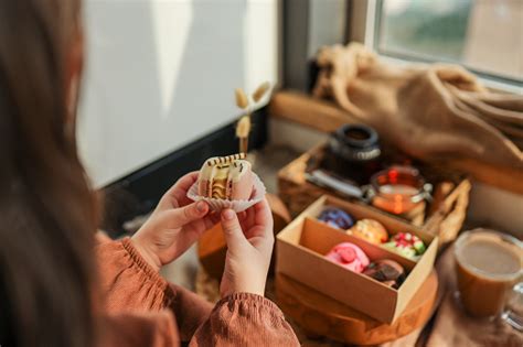 그녀의 손에 마카롱을 들고 아늑한 가정 분위기에서 배경에 모듬 마카롱 상자를 들고 있는 소녀 가꿔주기에 대한 스톡 사진 및 기타