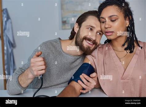 Cheerful Man Measuring Blood Pressure Of Pregnant African American Wife