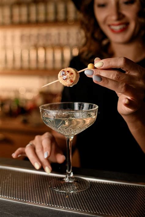 Cute Smiling Female Bartender Holding Skewer With Banana And Fried Sugar On It Over Glass Stock