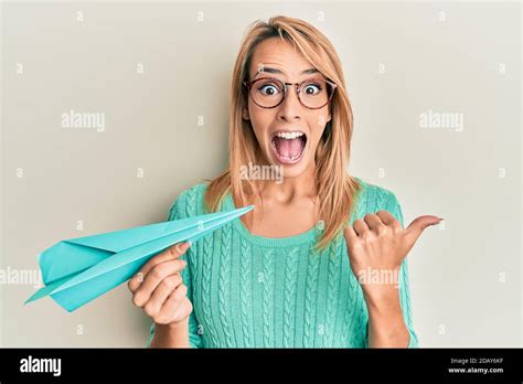 Beautiful Blonde Woman Holding Paper Airplane Pointing Thumb Up To The