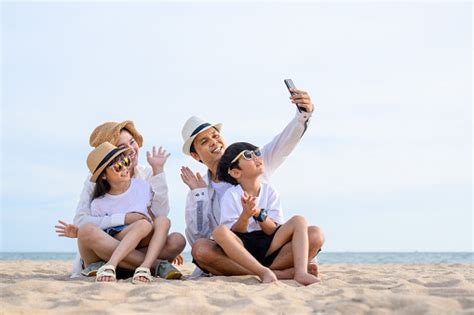 해변에서 셀카를 찍는 행복한 아시아 가족 해변 여행에서 함께 즐거운 시간을 보내는 가족 해변 휴가 중인 가족 자유와 여행 개념