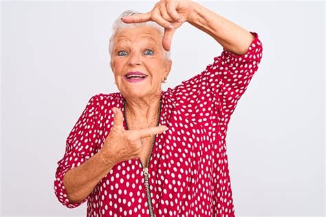 행복한 얼굴로 손과 손가락으로 프레임을 만드는 고립 된 흰색 배경 위에 서있는 빨간 캐주얼 재킷을 입은 선임 회색 머리 여성 창의력과 사진 개념 개념에 대한 스톡 사진 및