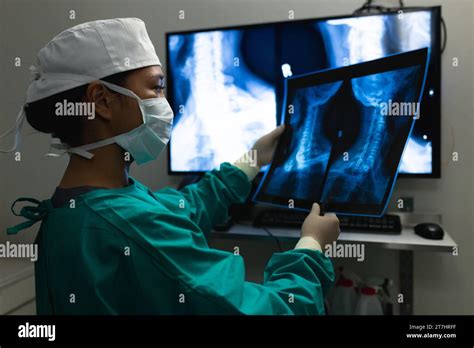 Asian Female Surgeon Looking At X Ray Scans In Operating Theatre At