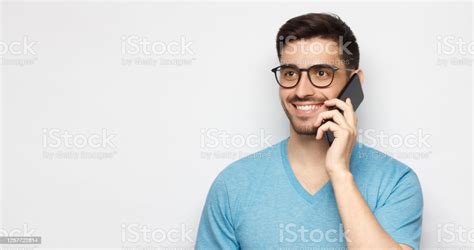 파란색 티셔츠를 입은 젊은 미소 짓는 남자의 수평 배너가 휴대 전화를 손에 들고 회색 배경에 고립 된 멀리 보고 있습니다 T