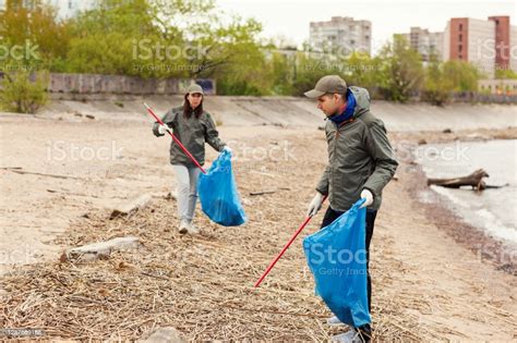 쓰레기 피커와 비닐 봉지를 사용하여 해안의 해변을 청소하는 두 명의 환경 운동가 젊은 남성과 여성 30 34세에 대한 스톡 사진