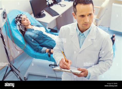 Serious Doctor Taking Notes During Electroencephalography Procedure