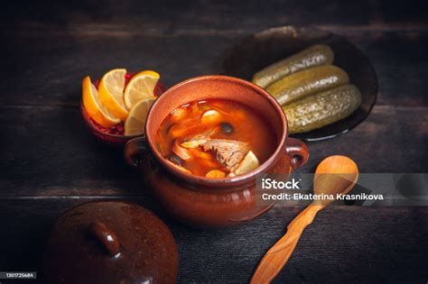 고기 소시지 야채 피클 올리브를 곁들인 수제 전통 러시아 수프 Solyanka와 짙은 나무 숟가락을 곁들인 세라믹 냄비에 레몬을