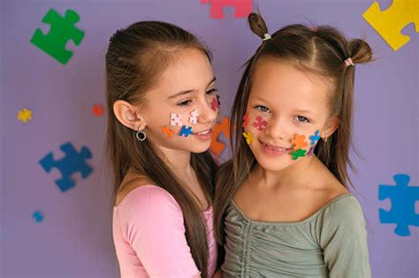 귀여운 자매들은 얼굴과 보라색 배경을 여러 가지 빛깔의 퍼즐 조각으로 장식했습니다 자폐증에 대한 인식의 날 증후군을 앓고 있는 아동의 행동과 교육의 어려움 4 5세에 대한