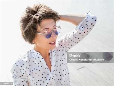 바람은 화려한 선글라스에 주근깨 여자의 짧은 머리를 주름 도시 공원의 열린 나무 장면에서 미소 짓는 여자 여름 분위기 진지한 감정 공원에 대한 스톡 사진 및 기타 이미지