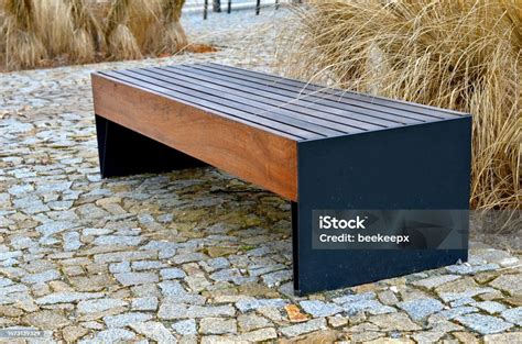 한쪽 다리에 금속 구호 구조가있는 나무 현대 공원 벤치는 휴게소와 베이지 색 자갈 잔디 다년생 화단의 작은 표면으로 만든 길에 공원에 서 있습니다 가을에 대한 스톡 사진 및