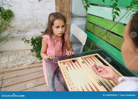 Young Girl Playing Backgammon Outdoors With Adult Learning And Focused