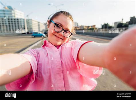Smiling Teenage Girl With Down Syndrome Taking Selfie On Street Stock