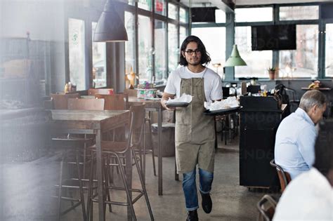 Full Length Of Young Waiter Serving Food While Walking By Customers In