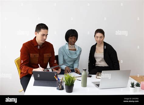 Three Focused Colleagues Are Collaborating On A Project Using Digital Tablets And Laptops At A