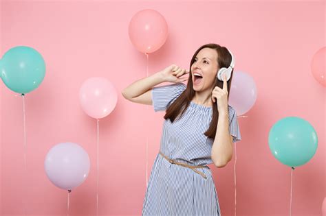 헤드폰을 화려한 공기 풍선 파스텔 핑크 배경에 파란 드레스 듣는 음악을 입고 좋아 라 행복 한 젊은 여자의 초상화 생일 휴가