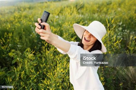 자연 필드 배경에 전화 Selfie를 복용 하는 흰 셔츠와 여자를 웃 고 있는 젊은 갈색 머리 아름 다운 미소의 위에서 볼