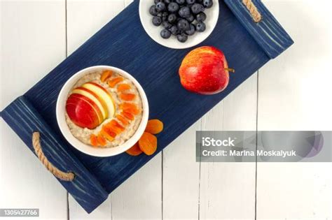 블루베리와 사과 슬라이스가 있는 죽 오트밀 그릇의 최고 전망 맛있는 건강한 아침 식사 파란색 트레이와 흰색 나무 테이블에 제공됩니다 목재 재료에 대한 스톡 사진 및 기타