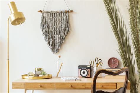 목조 책상 회색 Macrame 디자인 액세서리 사진 카메라 골드 램프와 흰색 벽에 나무 사다리와 세련 된 Scanidnavian