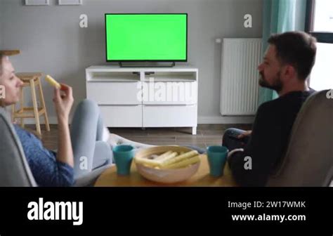 Man And Woman Are Sitting In Chairs Watching Tv With A Green Screen