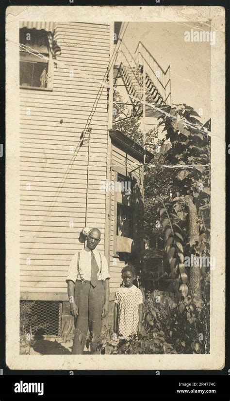 Unidentified Man And Girl Standing In Front Of A Dwelling With A Fire